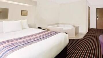 Quarto de hotel com uma cama grande, banheiro separado com banheira e carpete listrado.