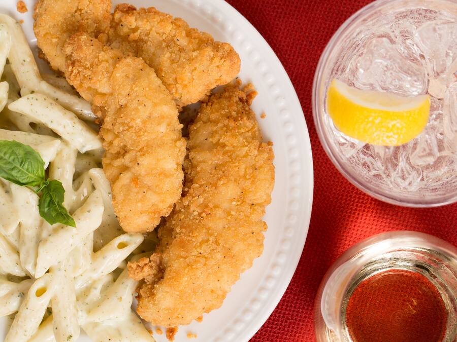Um prato de escalopes de frango empanados com massa e um copo de bebida gelada com uma fatia de limão.