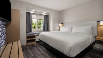 Quarto de hotel com uma cama grande, um banco com espaço de armazenamento, televisão e uma janela com cortinas.