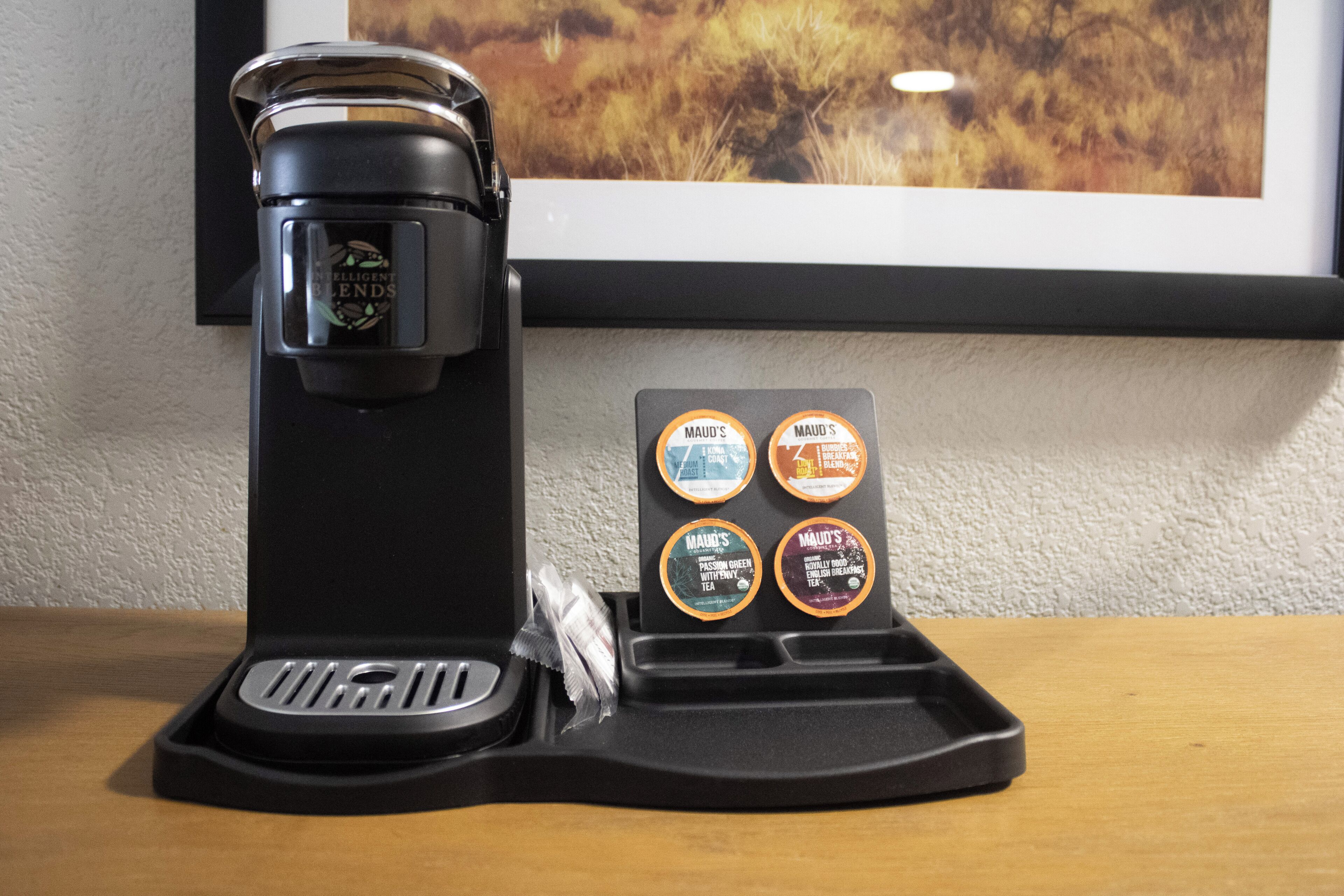 Uma cafeteira com base preta e recipiente de vidro, acompanhada por uma bandeja com quatro cápsulas de café rotuladas "Maui's".