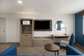 Quarto moderno com televisão de tela plana na parede, uma pequena escrivaninha com cadeira, micro-ondas em armário e sofá azul.