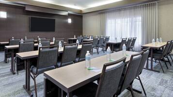 Uma sala de conferências de hotel com várias mesas e cadeiras, equipada com garrafas de água e blocos de notas.