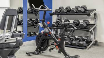 Uma academia com equipamentos de exercícios, incluindo uma bicicleta ergométrica, halteres e uma esteira.