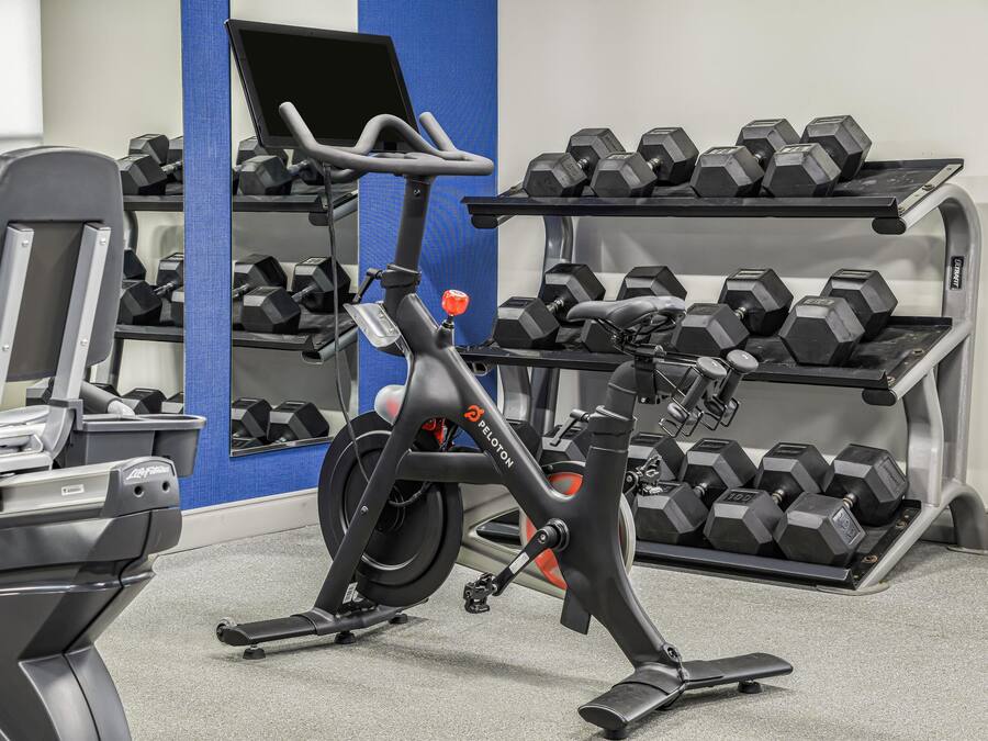 Uma academia com equipamentos de exercícios, incluindo uma bicicleta ergométrica, halteres e uma esteira.