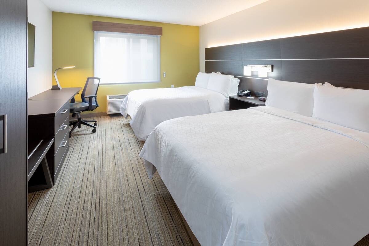 Quarto de hotel com duas camas, uma escrivaninha, uma cadeira e uma mesa de cabeceira com abajur.