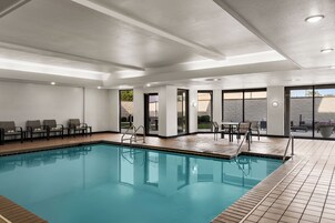 Piscina com deck revestido, cadeiras e mesas para relaxamento.