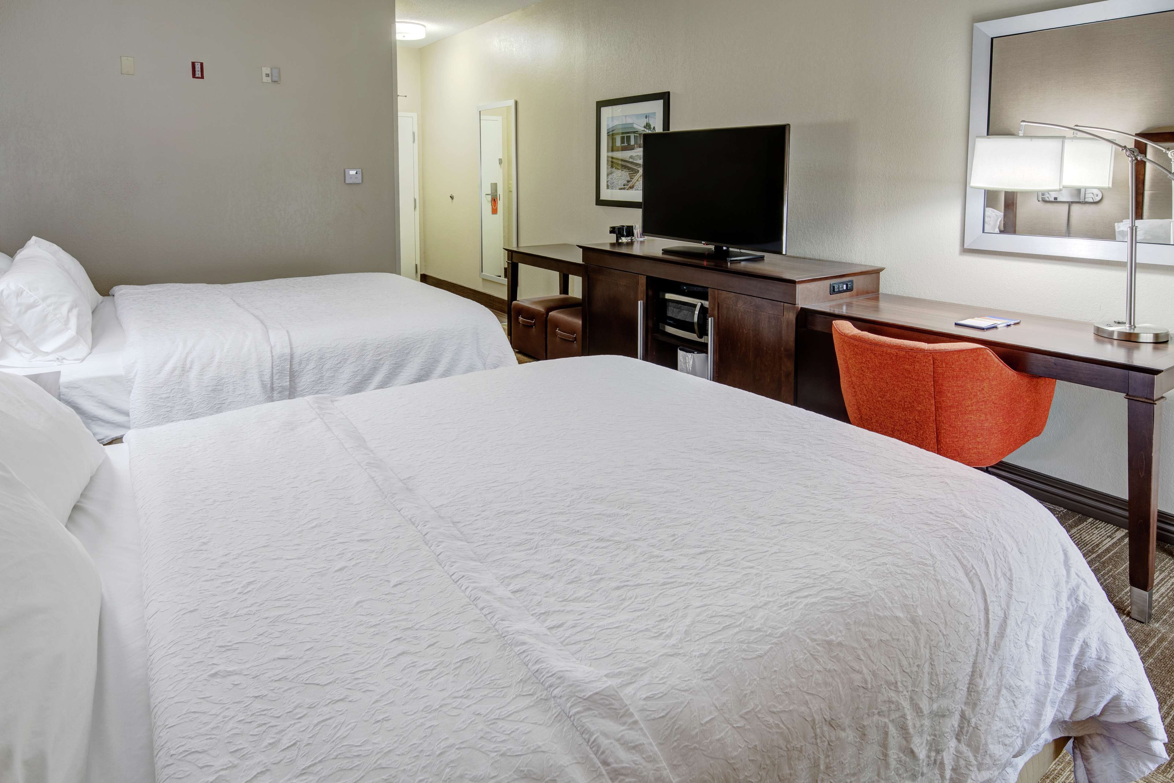 Quarto de hotel com duas camas, uma escrivaninha, uma televisão e um espelho.