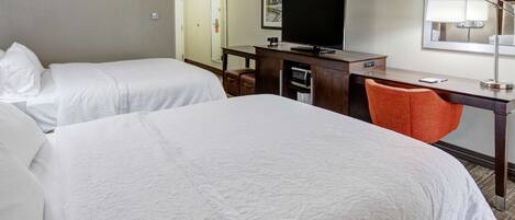 Quarto de hotel com duas camas, uma escrivaninha, uma televisão e um espelho.