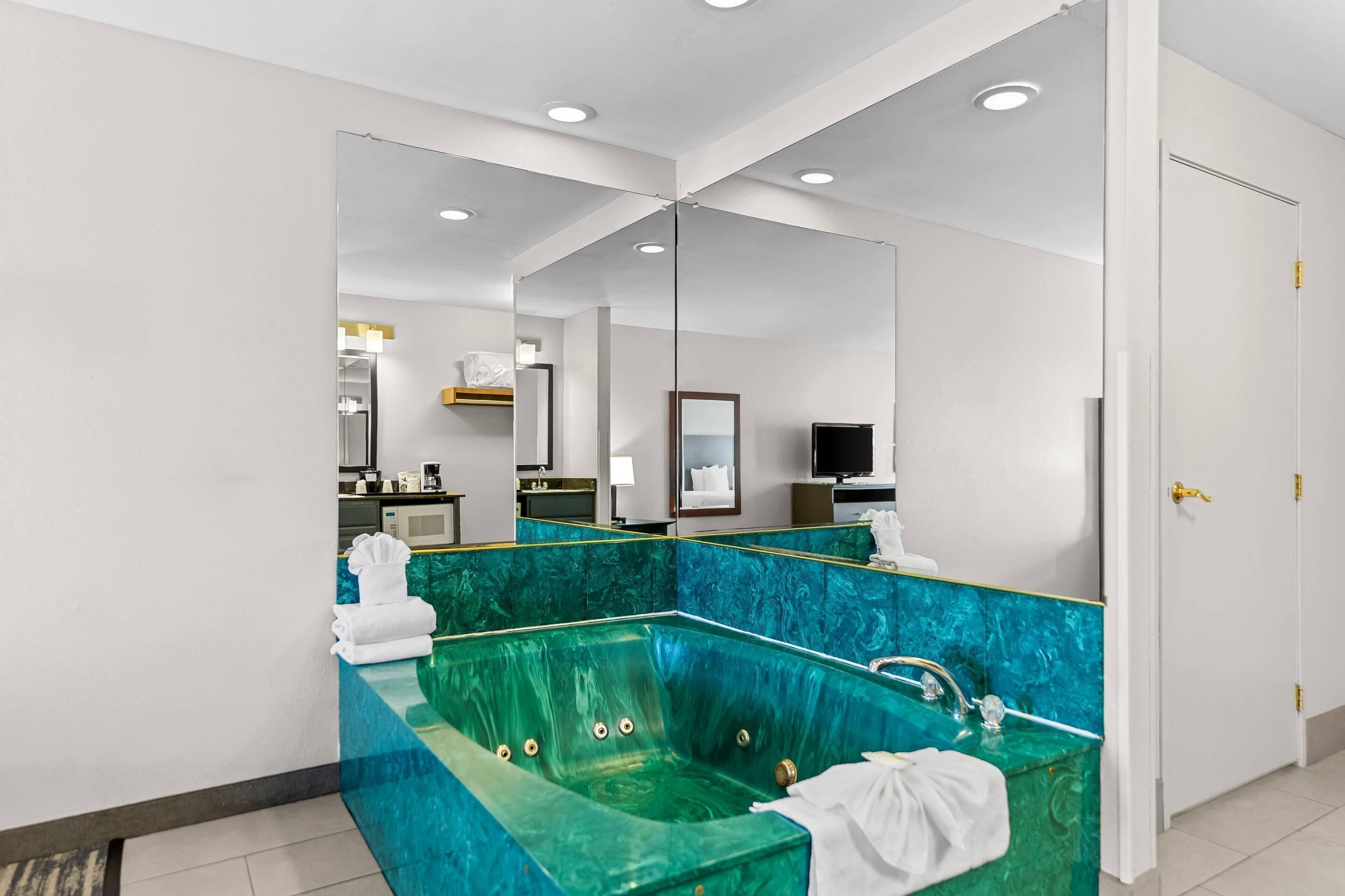 Um banheiro moderno com uma grande banheira de hidromassagem verde, um espelho grande e uma porta branca.
