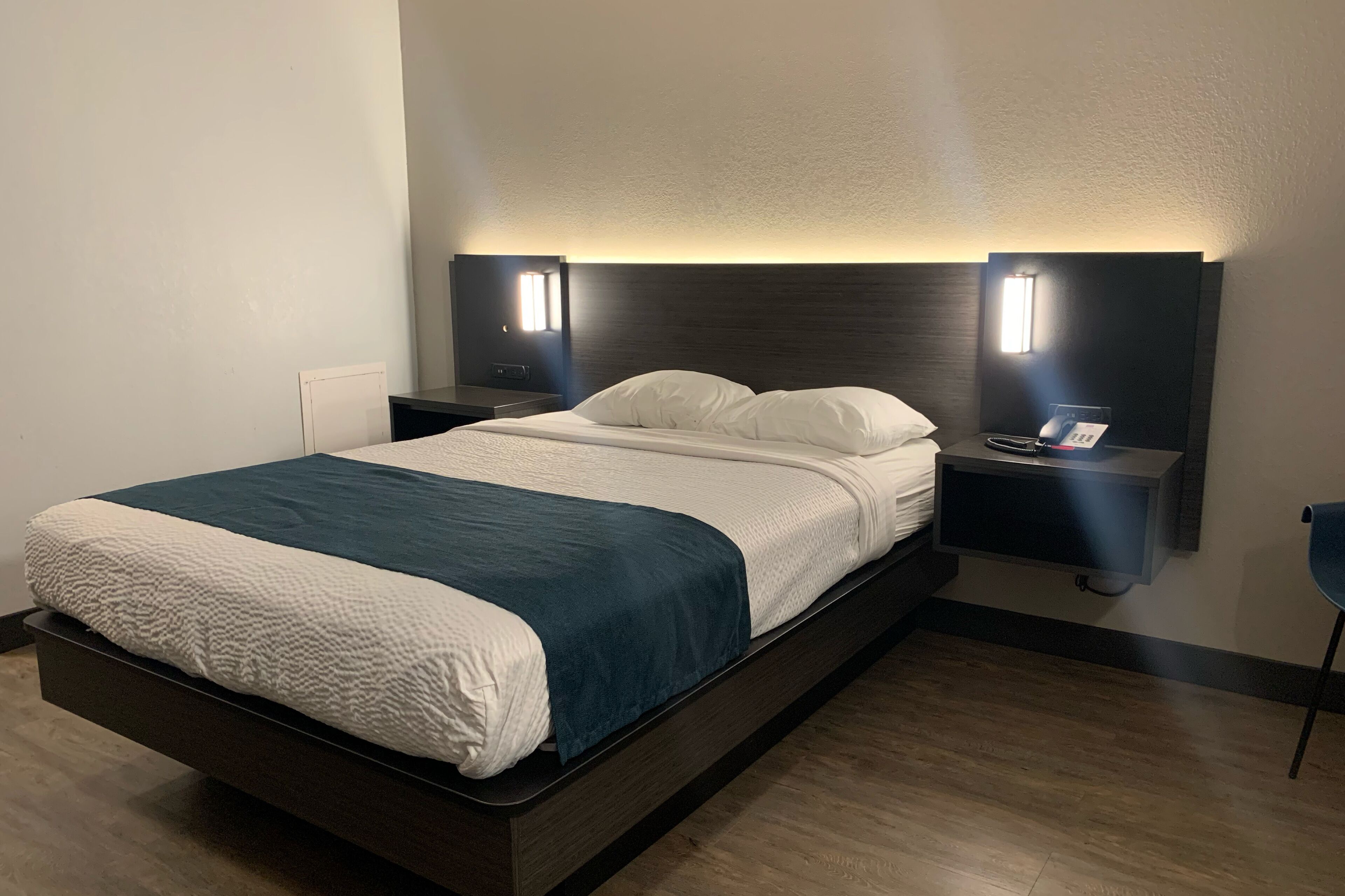 Quarto de hotel moderno com uma cama grande, duas mesas de cabeceira, televisão de tela plana e iluminação embutida na parede.