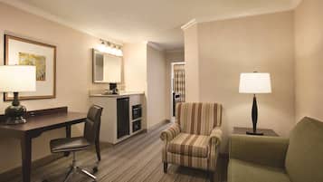 Quarto de hotel com escrivaninha, cadeira, poltrona listrada e sofá verde.
