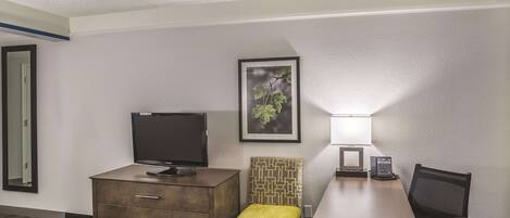 Quarto de hotel com escrivaninha, cadeira, televisão e um quadro na parede.