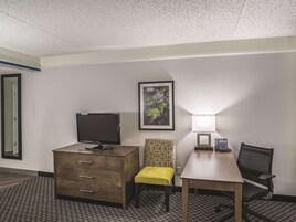 Quarto de hotel com escrivaninha, cadeira, televisão e um quadro na parede.