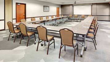 Uma sala de conferências com uma mesa comprida, cadeiras, um projetor e piso coberto de carpete.
