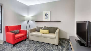 Uma sala de estar moderna com uma poltrona vermelha, um sofá bege, uma televisão de tela plana e um abajur.