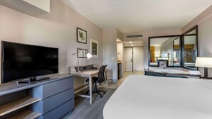 Quarto de hotel com cama, escrivaninha com computador, televisão e um espelho grande.