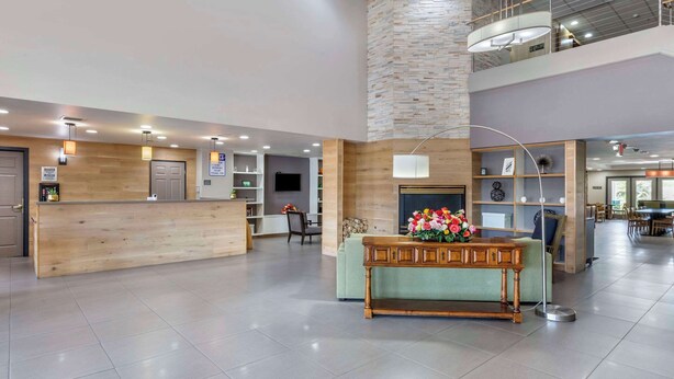 Um hall amplo com balcão de recepção, área de estar com mesa de madeira e flores, e escada para um andar superior.