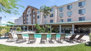 Um hotel com piscina, espreguiçadeiras e um espaço de estar coberto.