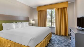 Quarto de hotel com cama grande, televisão, escrivaninha e janela com cortinas.