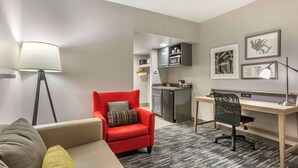 Quarto de hotel compacto com cozinha compacta, uma poltrona vermelha, uma escrivaninha e uma luminária.