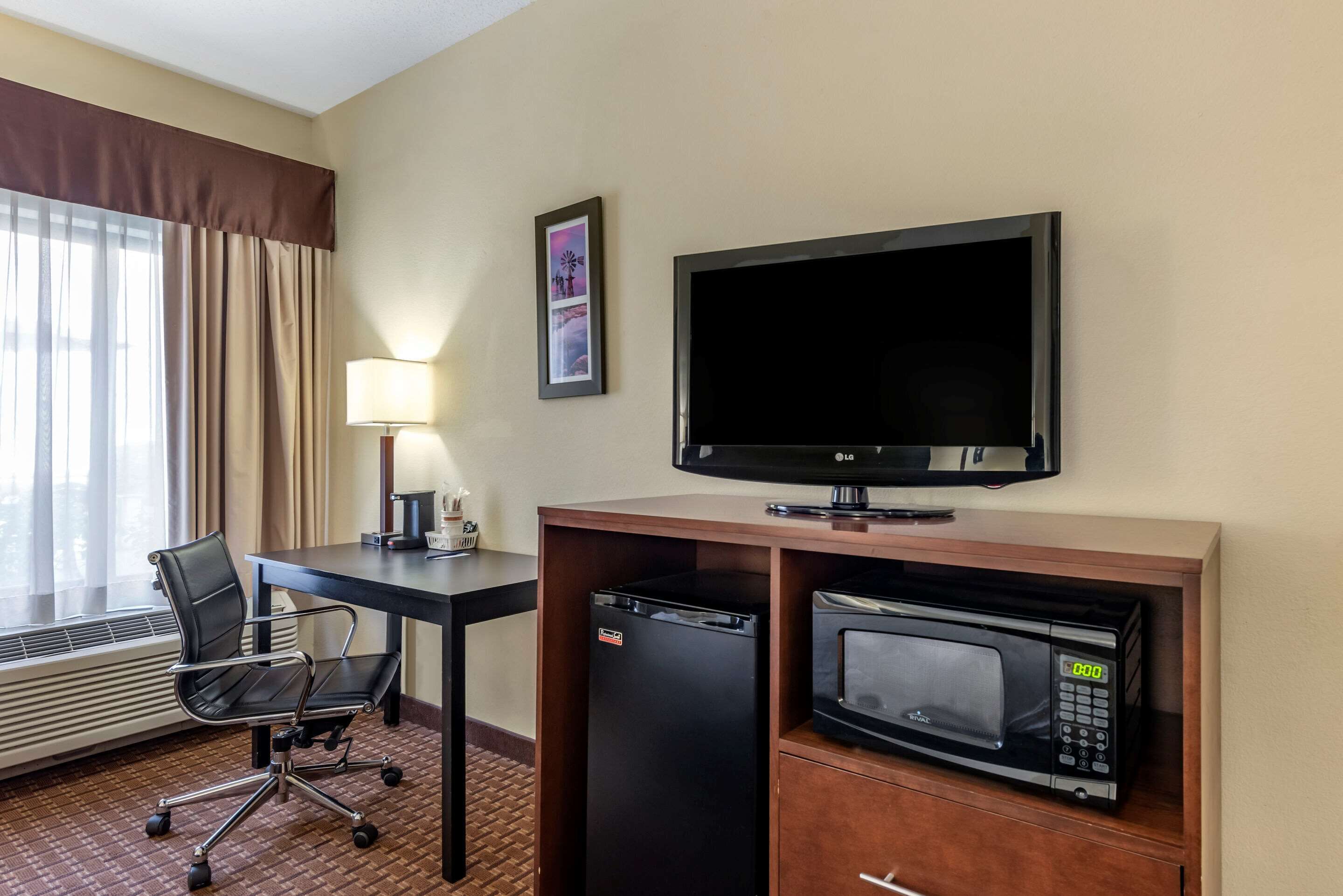 Quarto de hotel com escrivaninha, cadeira, televisão, frigorífico e micro-ondas.