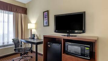 Quarto de hotel com escrivaninha, cadeira, televisão, frigorífico e micro-ondas.