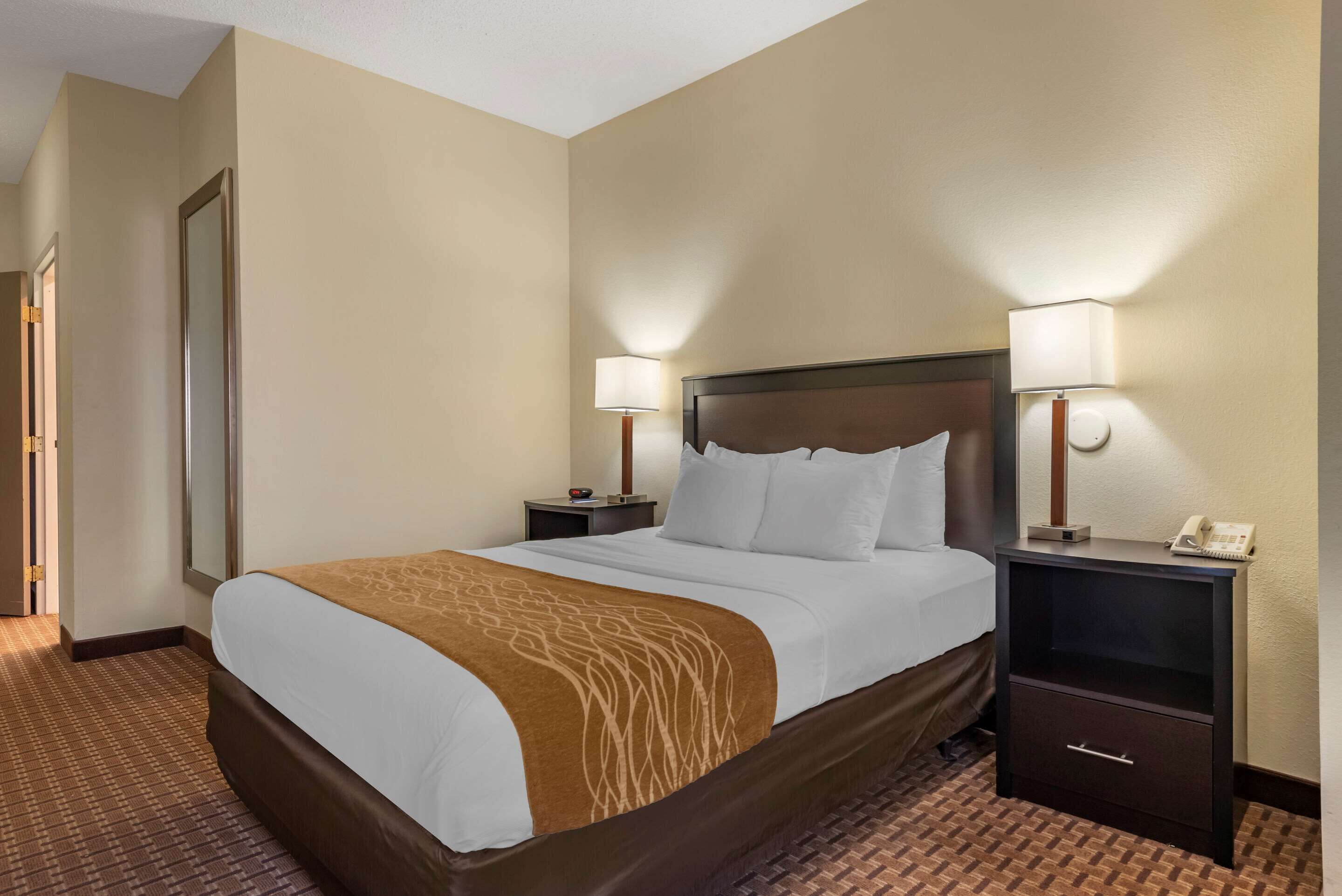 Quarto de hotel com uma cama grande, duas mesas de cabeceira com abajures, uma mesinha de apoio e um telefone.