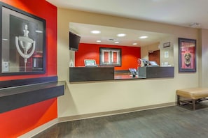 Uma área de recepção com balcão, um banco, uma moldura com imagem e uma janela com cortinas vermelhas.