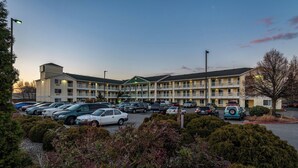 Um motel com vários andares e um estacionamento cheio de carros, rodeado por áreas ajardinadas.
