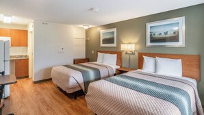 Quarto de hotel com duas camas, uma cozinha compacta e banheiro.