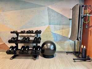 Uma academia com um suporte de halteres fixado na parede, uma bola de exercícios grande e uma barra para barra fixa.