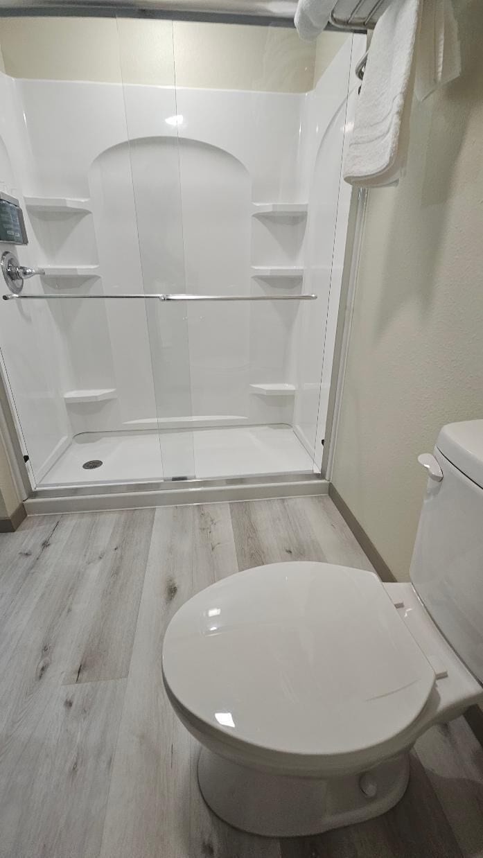Casa de banho com sanita, cabine de duche com vidro e chão em mosaico branco.