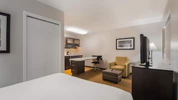 Quarto de hotel com cama, escrivaninha, cadeira, televisão e frigobar.