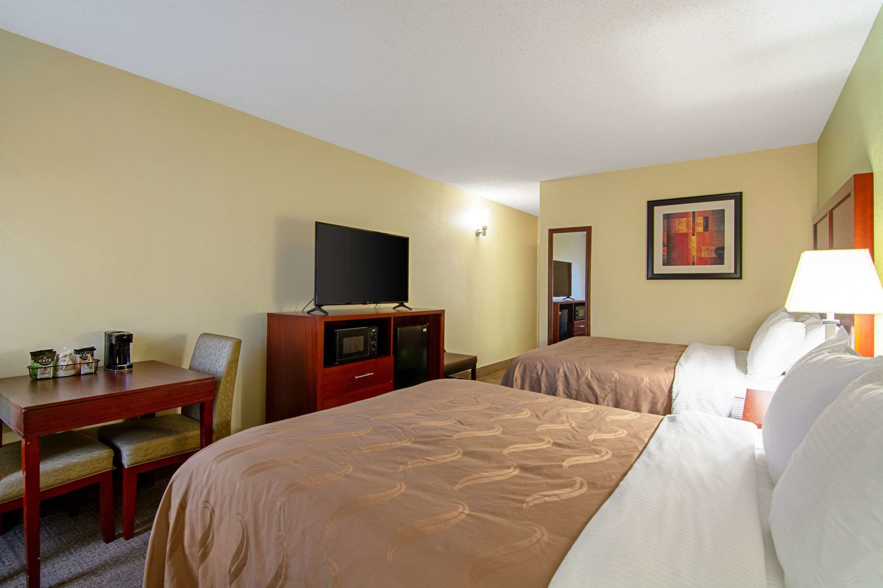 Quarto de hotel com duas camas, uma escrivaninha com televisão, micro-ondas e máquina de café.