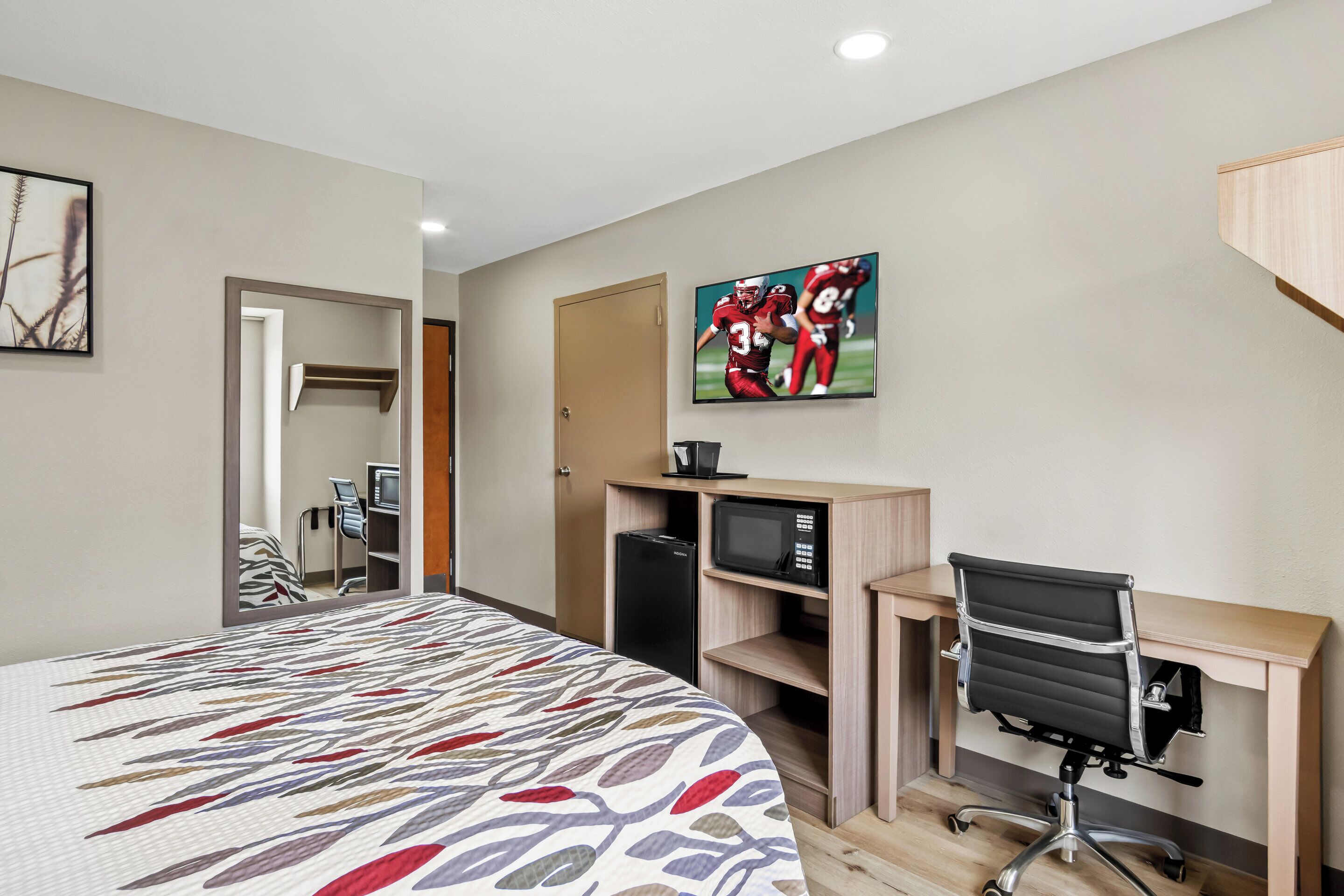 Quarto de hotel com cama, escrivaninha com computador, televisão e micro-ondas.
