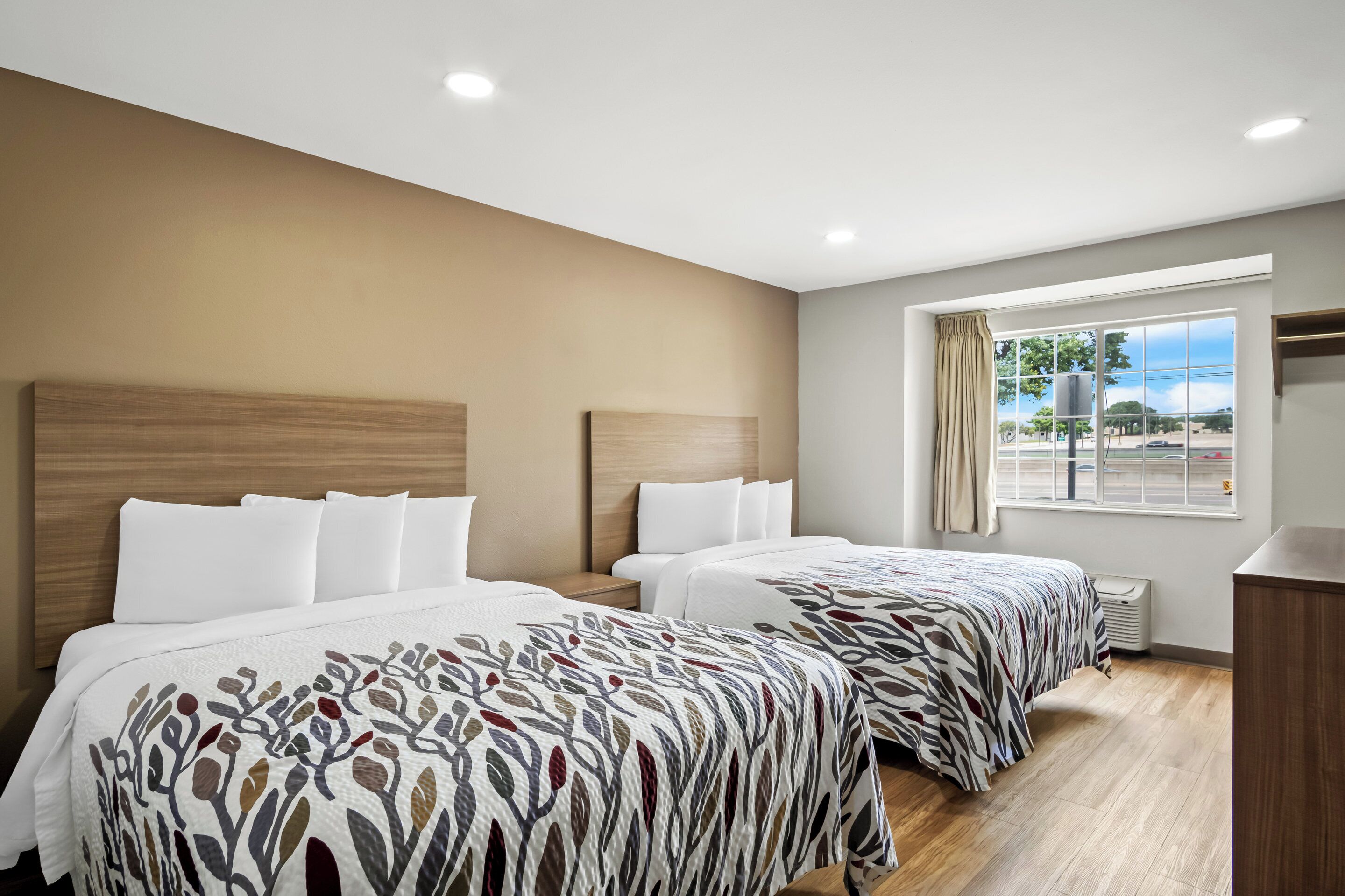 Quarto de hotel com duas camas, uma janela ampla e vista, e cabeceira de madeira.