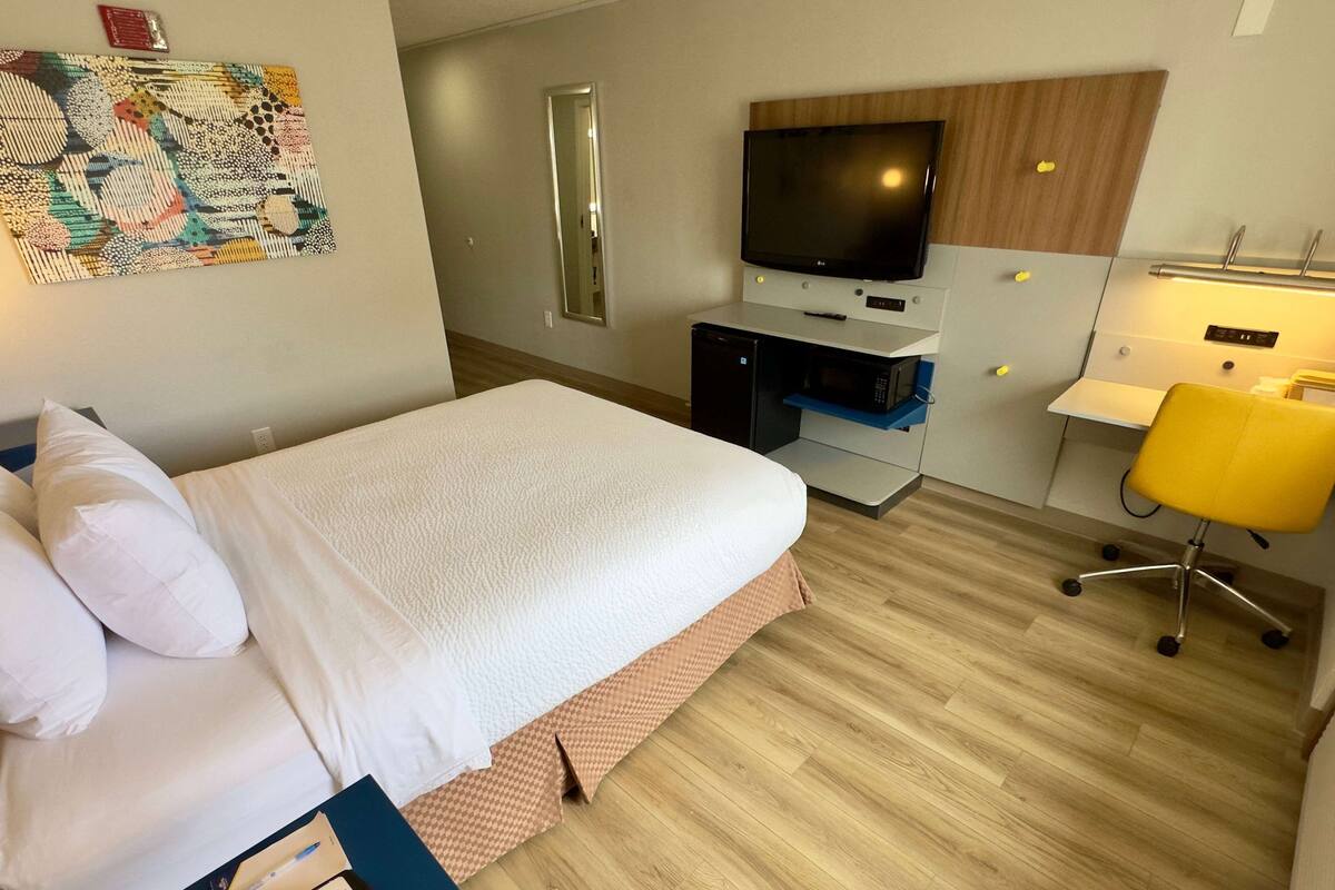 Quarto de hotel com cama, escrivaninha, televisão e cadeira.