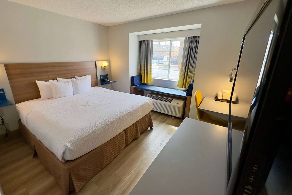 Quarto de hotel com uma cama grande, uma escrivaninha, uma cadeira, uma televisão e uma janela com cortinas.