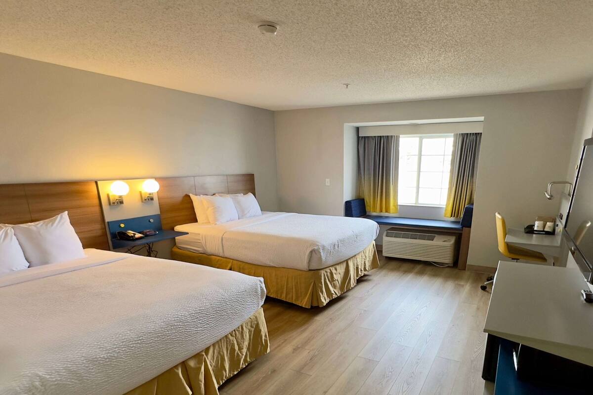 Quarto de hotel com duas camas, uma escrivaninha e uma janela com cortinas.