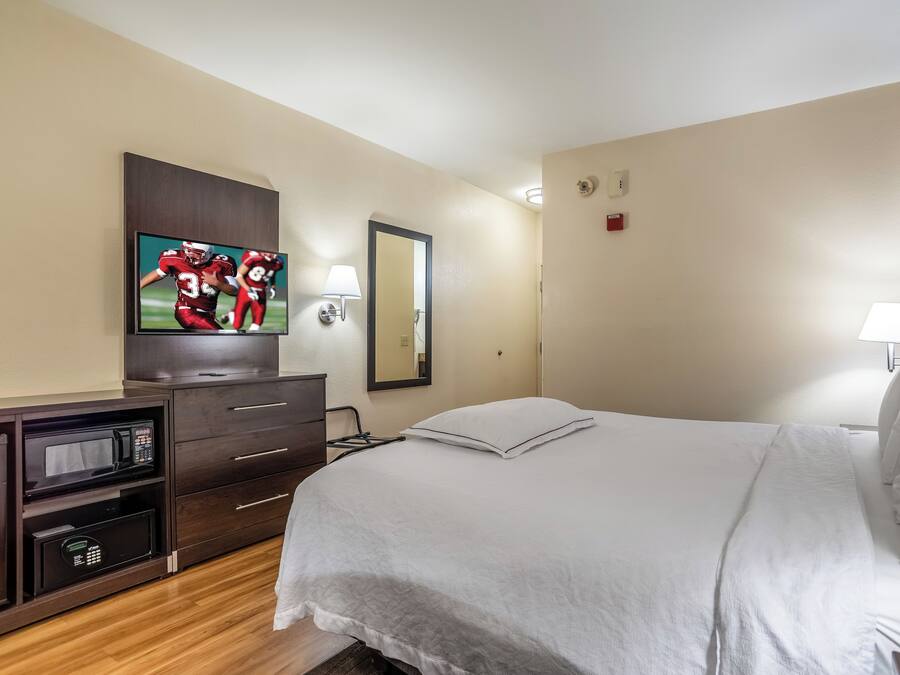 Quarto de hotel com cama, televisão, cômoda com micro-ondas e espelho.