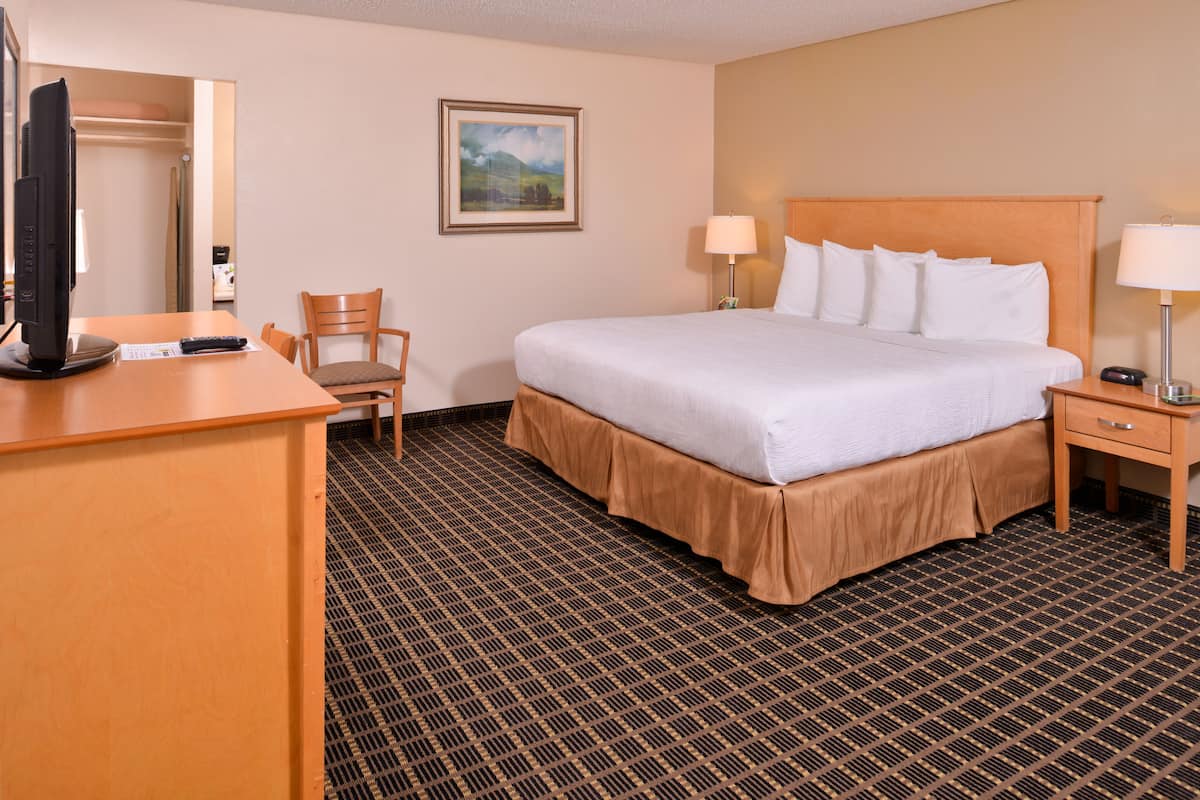 Quarto de hotel com uma cama grande, uma mesa com computador, uma cadeira e uma televisão.