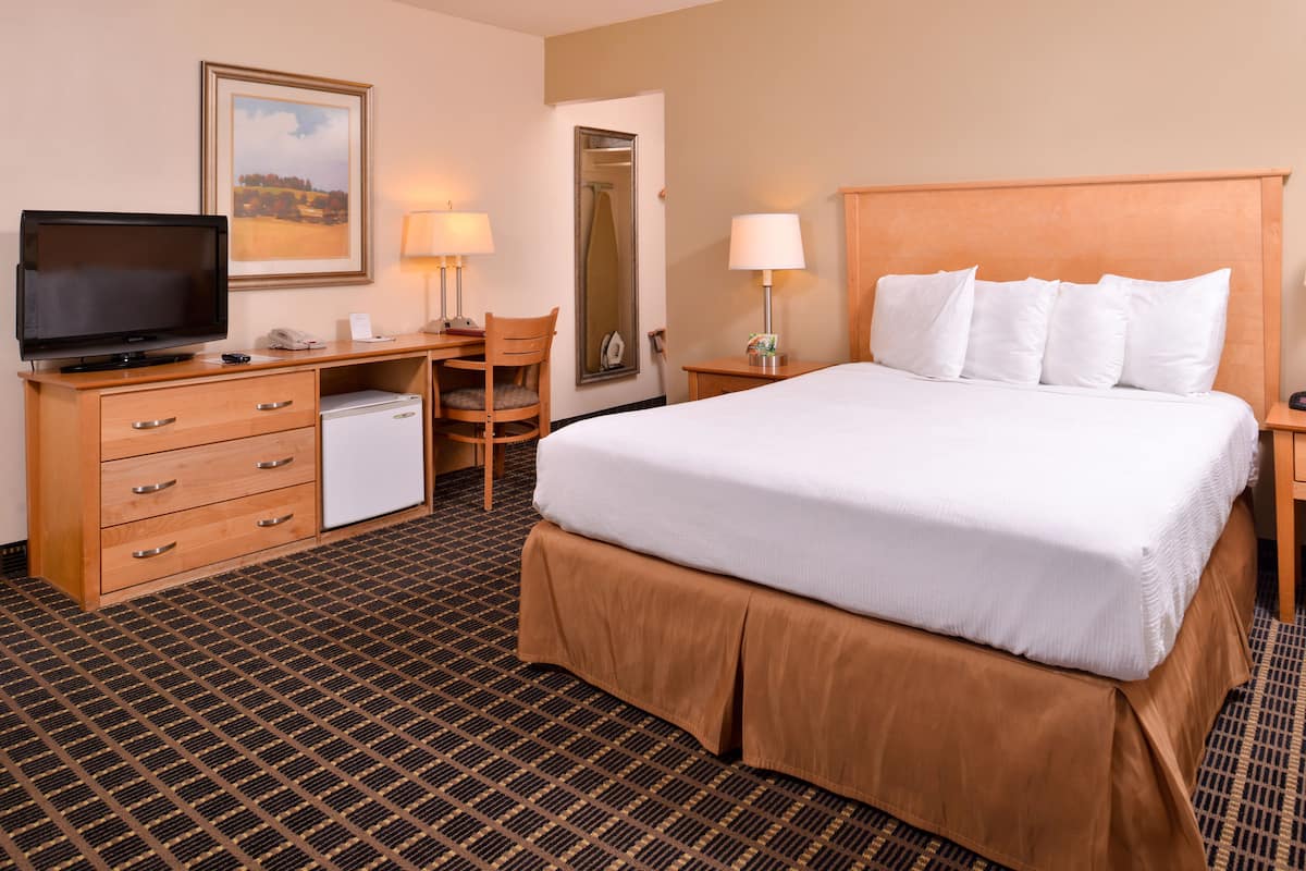 Quarto de hotel com cama, escrivaninha com computador, televisão e mini-frigorífico.