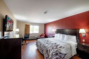 Quarto de hotel com cama, escrivaninha, cadeira e televisão na parede.
