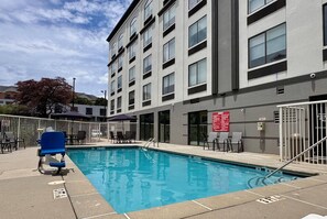 Uma piscina com espreguiçadeiras, um edifício com várias janelas e um letreiro na parede.