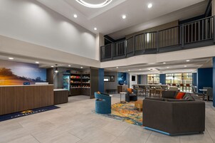 Um hall amplo com balcão de recepção, área de estar com sofá e cadeiras, escada e sala de jantar com mesas e cadeiras.