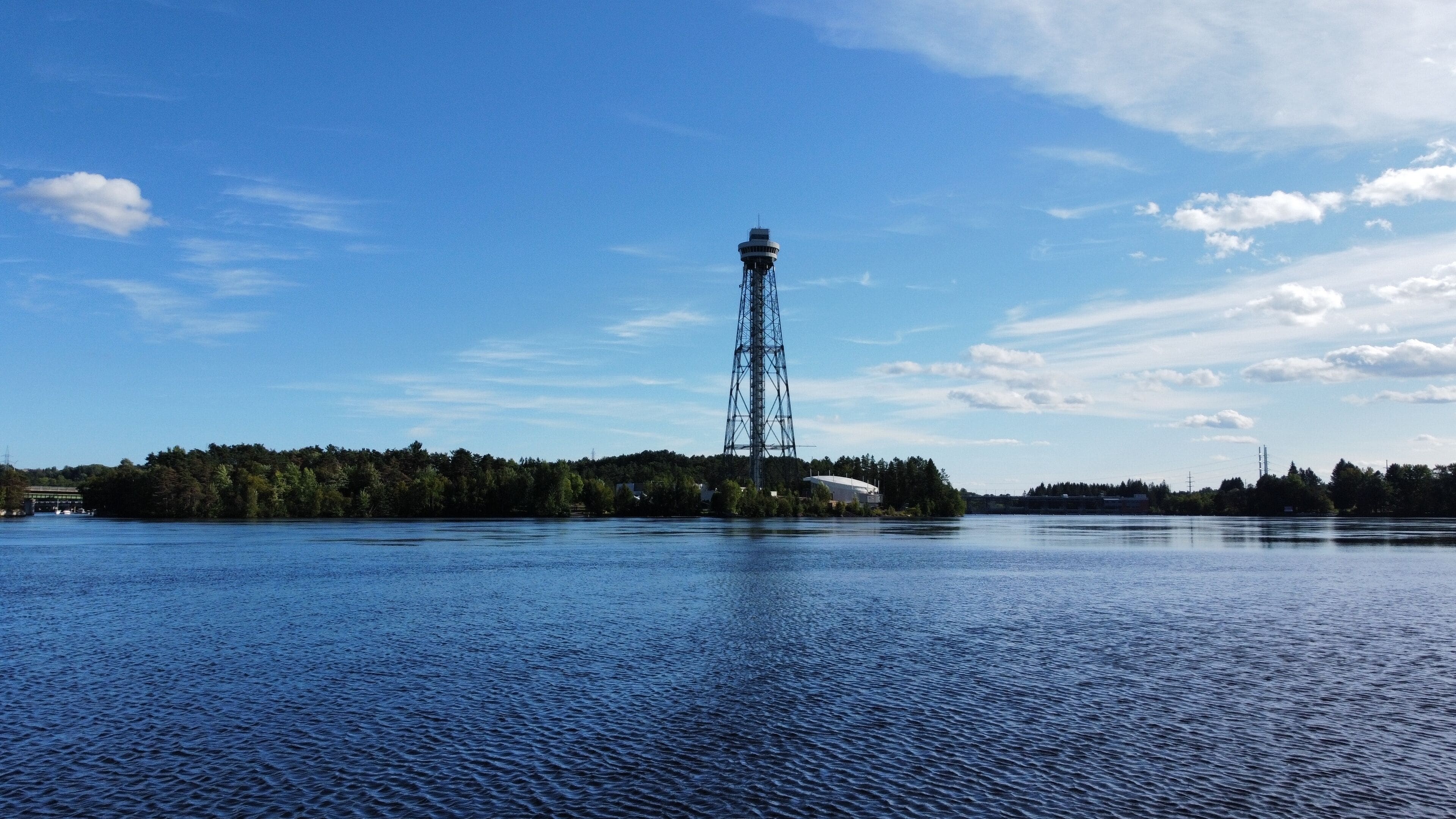 Um lago calmo com uma alta torre de comunicação no centro.