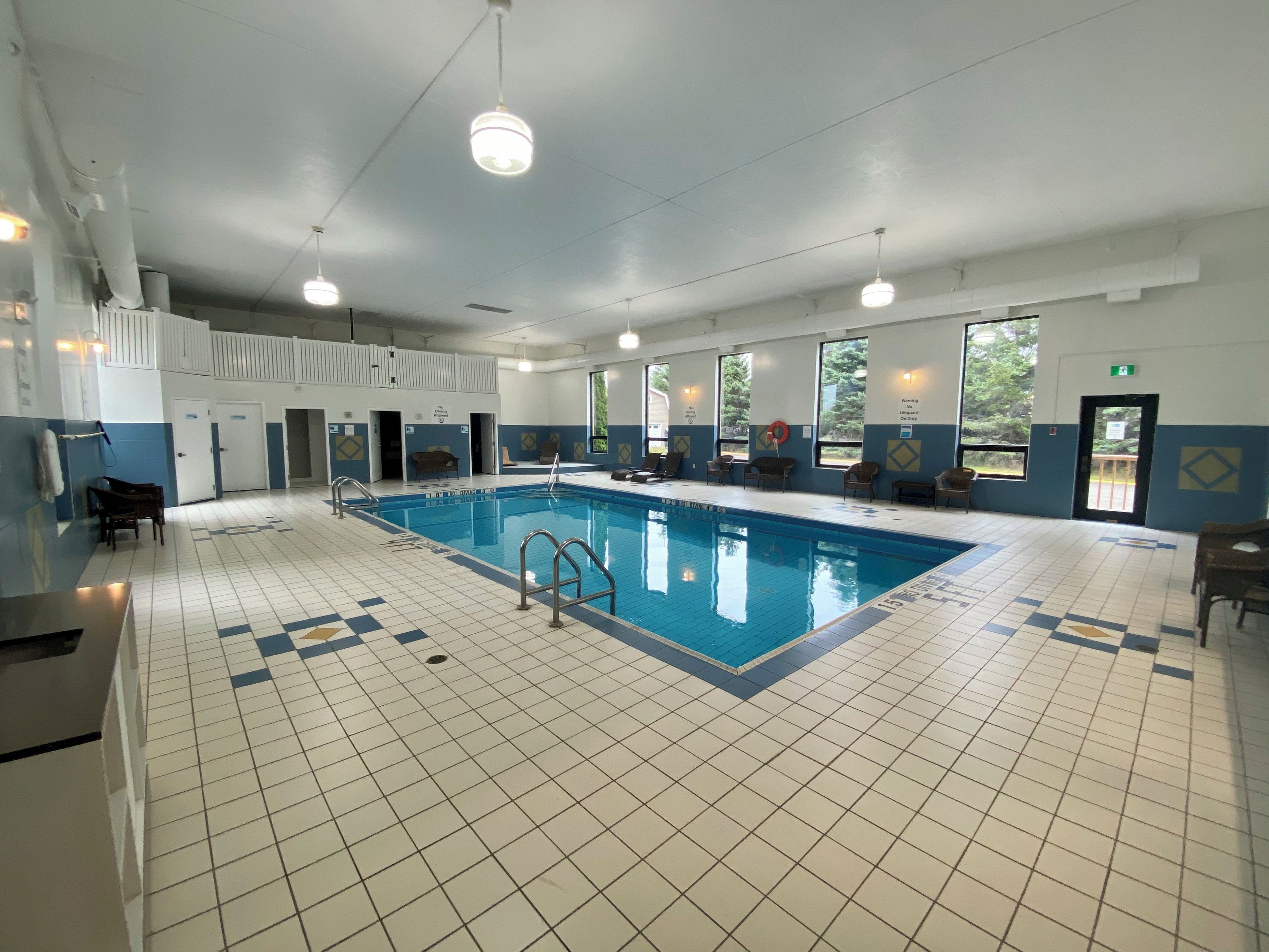 Piscina interna com piso ladrilhado, área de estar e janelas.
