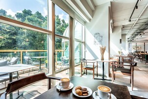 Um café moderno com janelas amplas, móveis de madeira e vista para uma floresta.