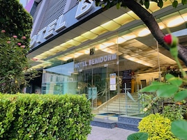 Uma entrada de hotel moderna com fachada de vidro, escadaria visível e placa com a inscrição 'HOTEL BENIDORM'.