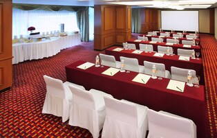 Sala de conferência com mesas preparadas para reuniões, equipada com garrafas de água e blocos de anotações.
